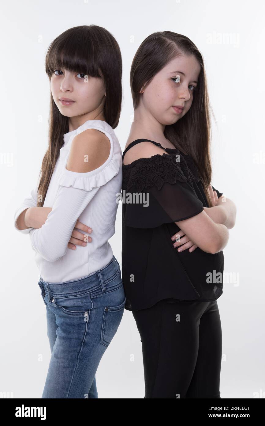 two female siblings stand back to back with arms crossed arms isolated ...