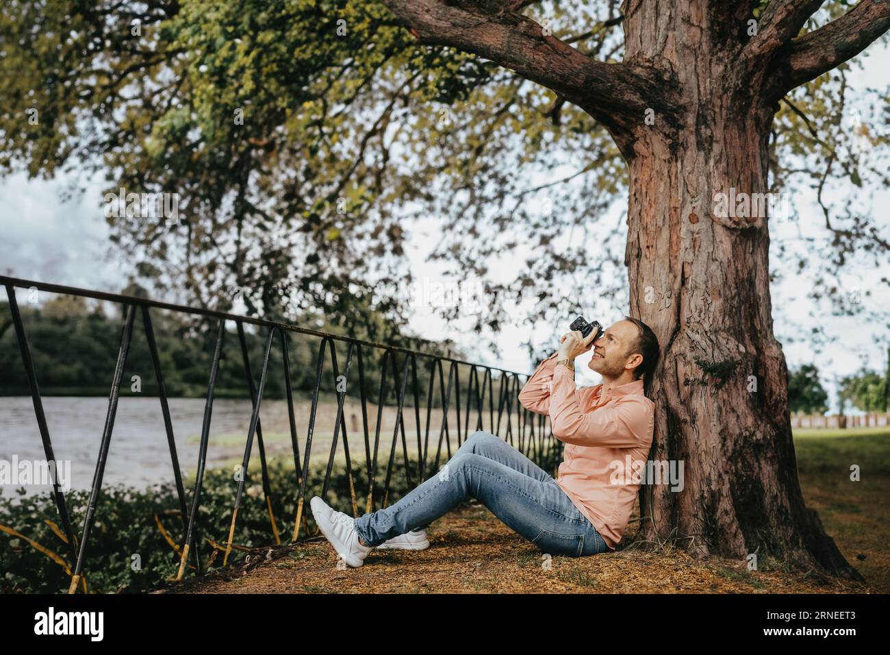 young man sit on ground lean to a tree and take photos with his old ...
