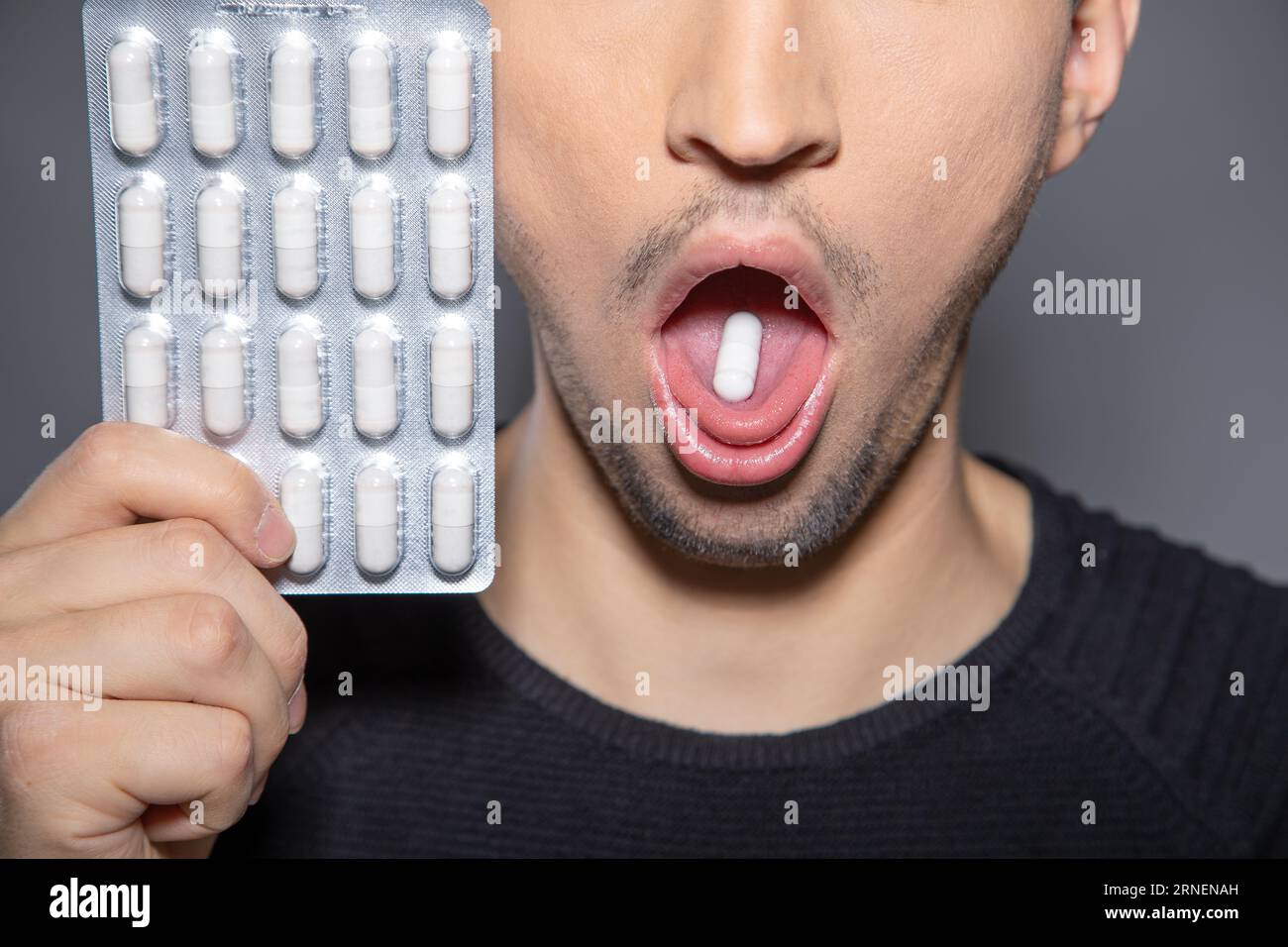 sick man with wide open mouth has capsule on his tongue and holds ...