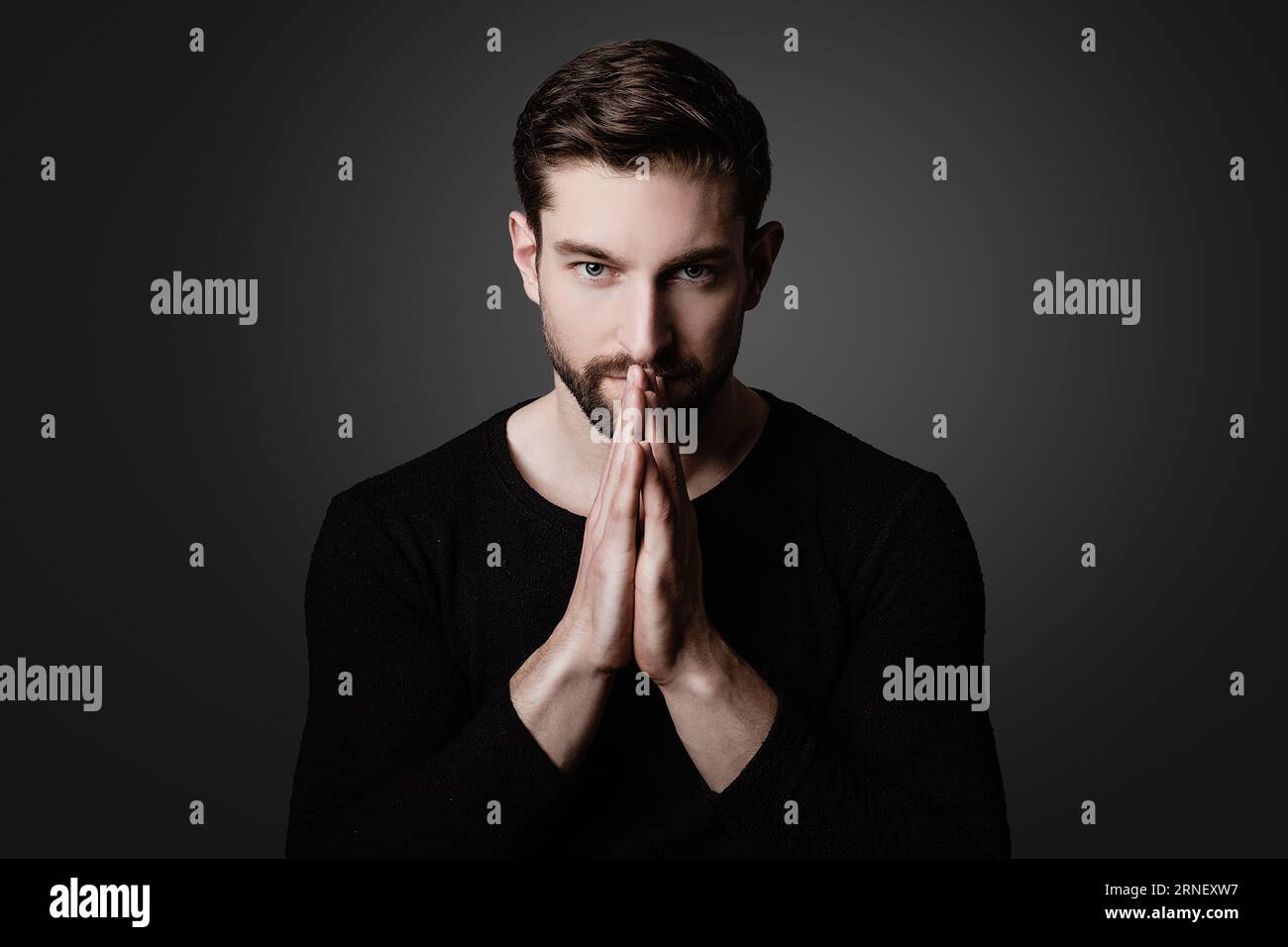 praying man with hands in front of face look at camera and pose while ...