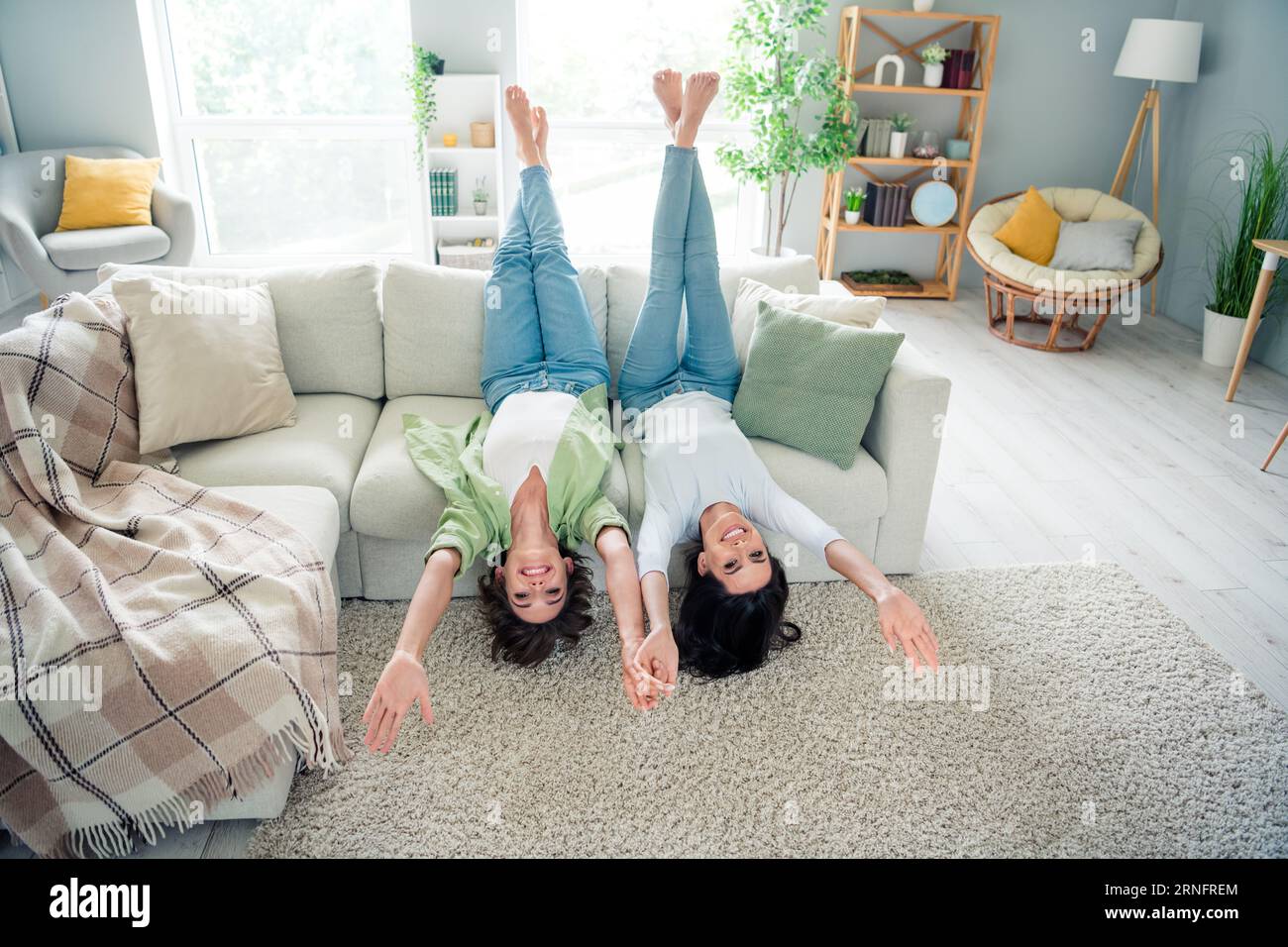 Full length photo of two overjoyed positive girls sit couch upside down ...