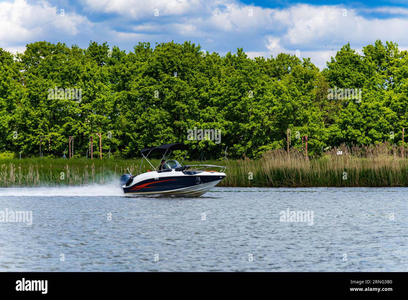 Very fast swimming small boat on wide river with green trees and bushes ...