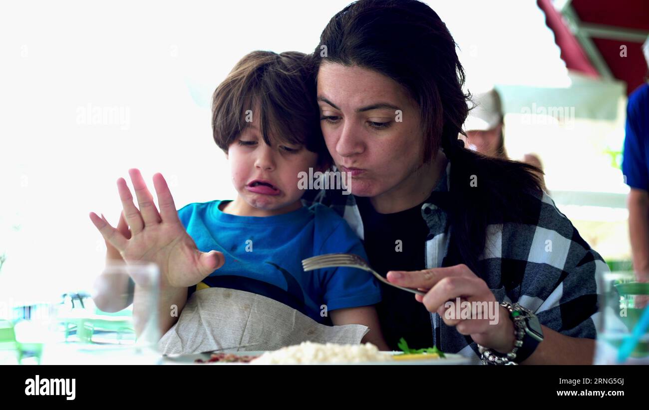 Mother feeding restless child at restaurant, kid sitting on mom's lap ...