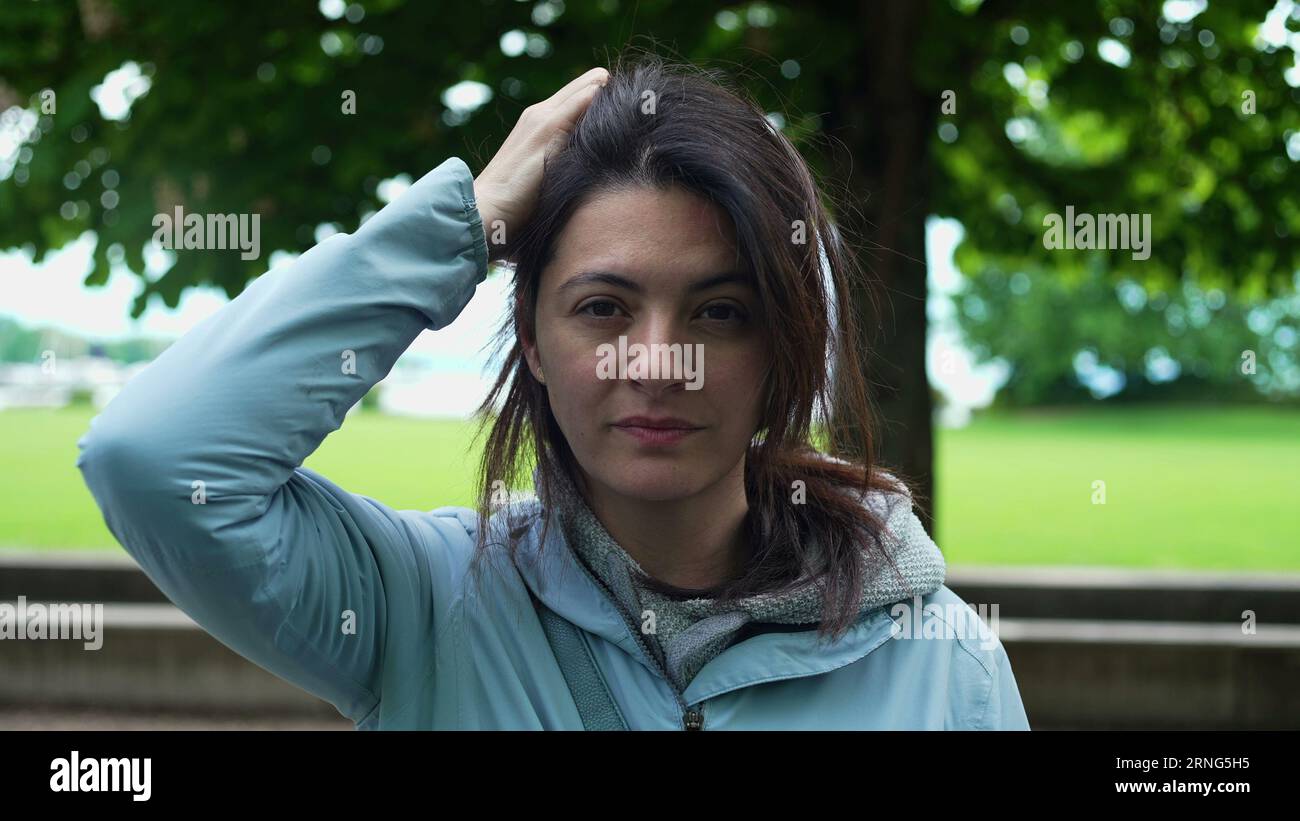 Disheveled carefree woman in 30s standing outside at park scratching ...