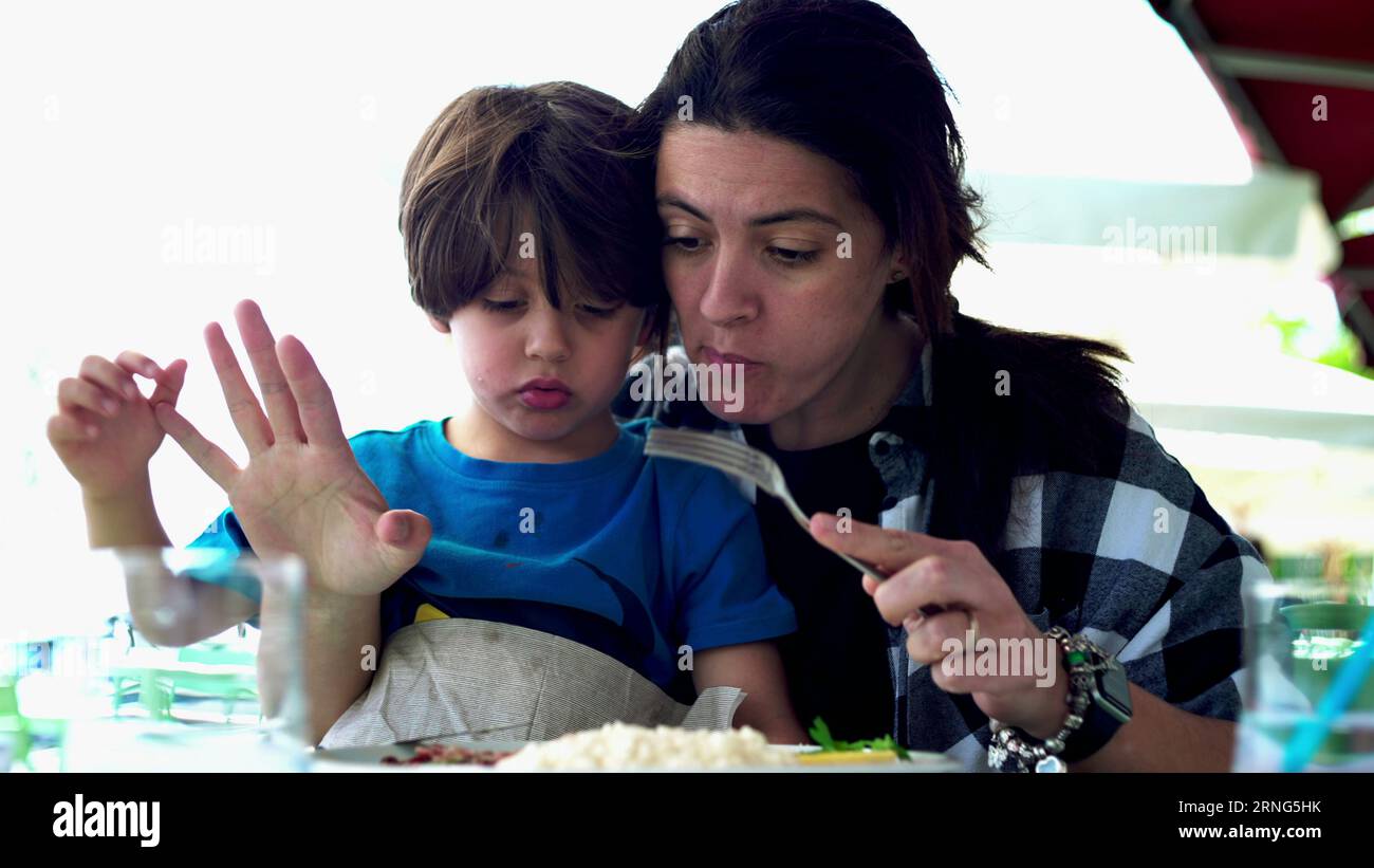 Mother feeding restless child at restaurant, kid sitting on mom's lap ...