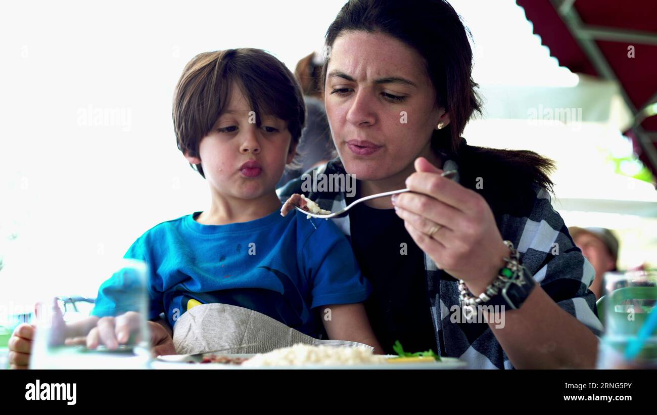 Mother feeding restless child at restaurant, kid sitting on mom's lap ...