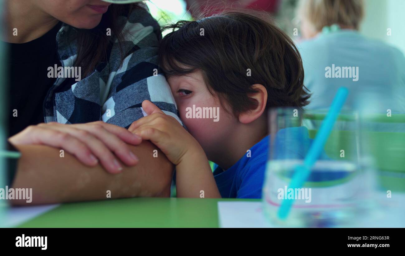 Bored small boy leaning on mother arm feeling boredom at restaurant waiting for food to arrive ...