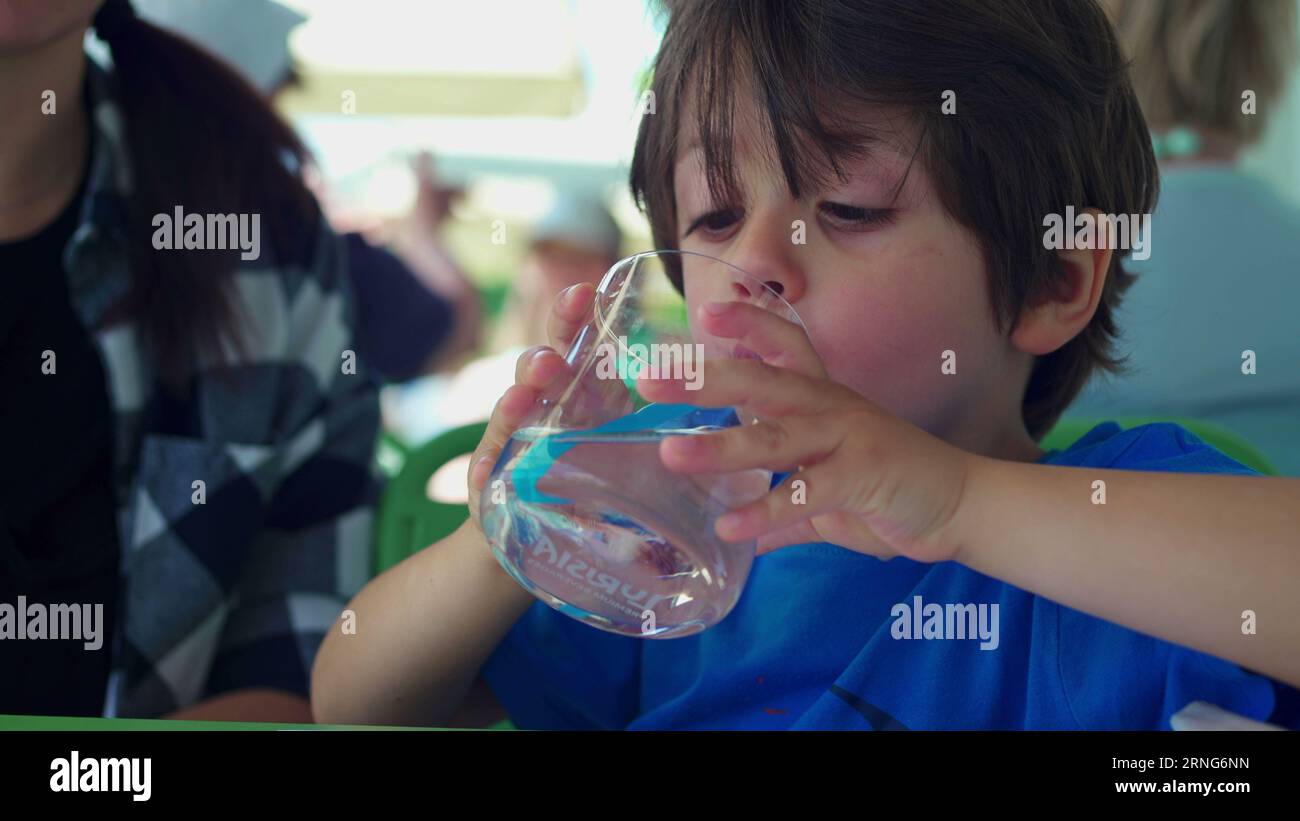 Small boy drinking water with straw at restaurant. Child close-up face ...