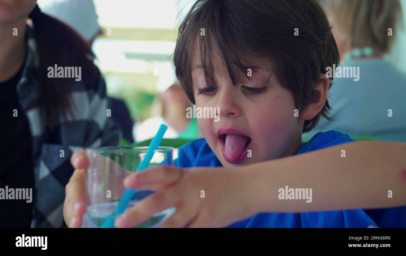 Small boy drinking water with straw at restaurant. Child close-up face ...