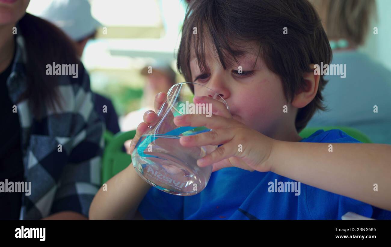 Small boy drinking water with straw at restaurant. Child close-up face ...