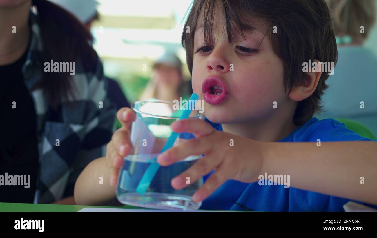 Small boy drinking water with straw at restaurant. Child close-up face ...