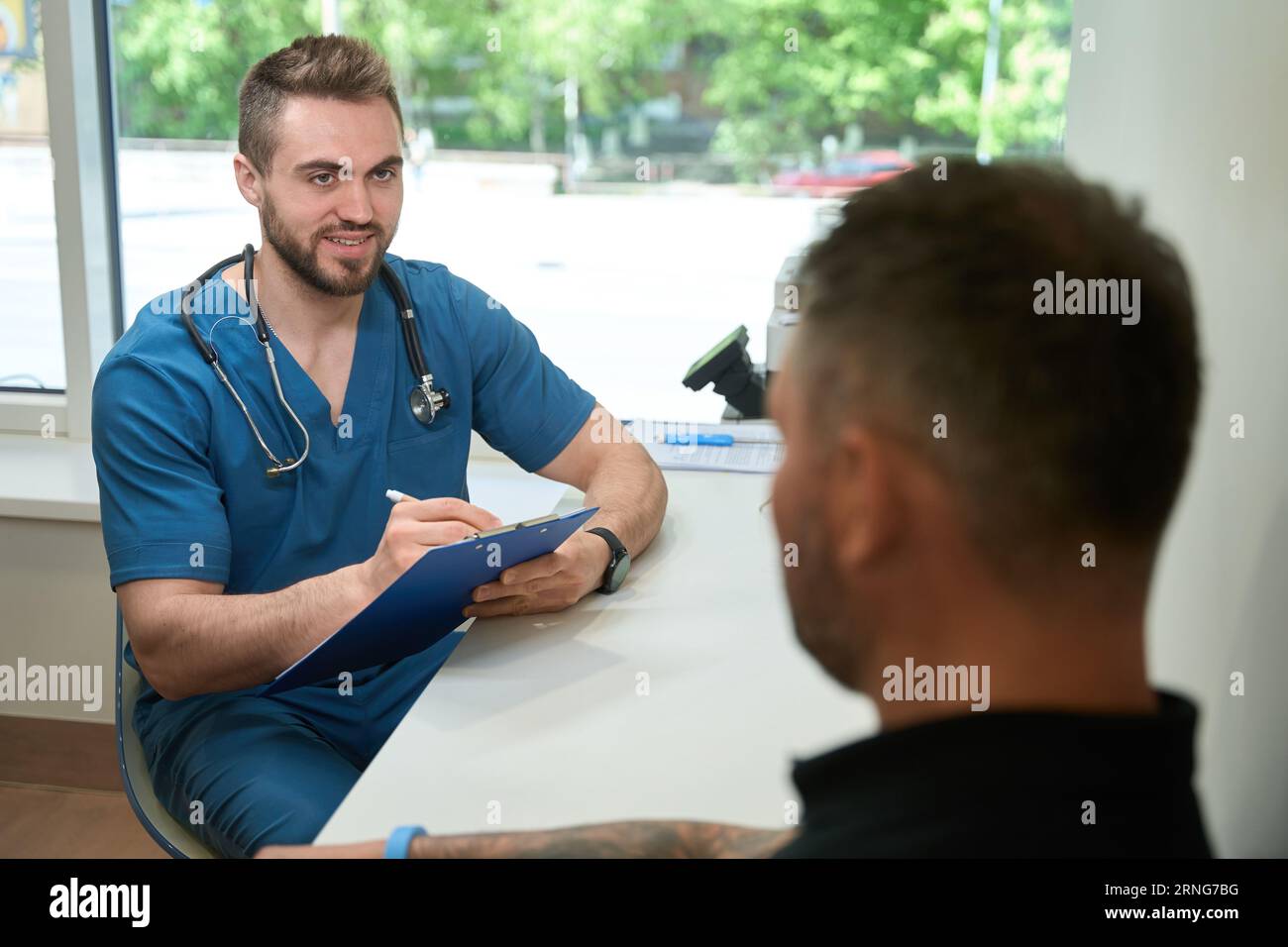 Friendly young physician taking notes during primary patient ...