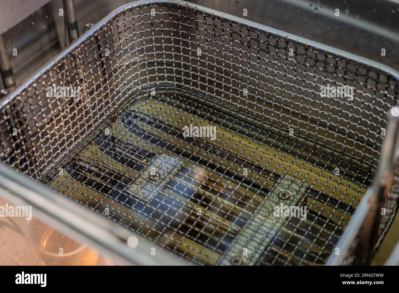 Empty industrial deep fryer filled with hot oil. Visible metal mesh or ...