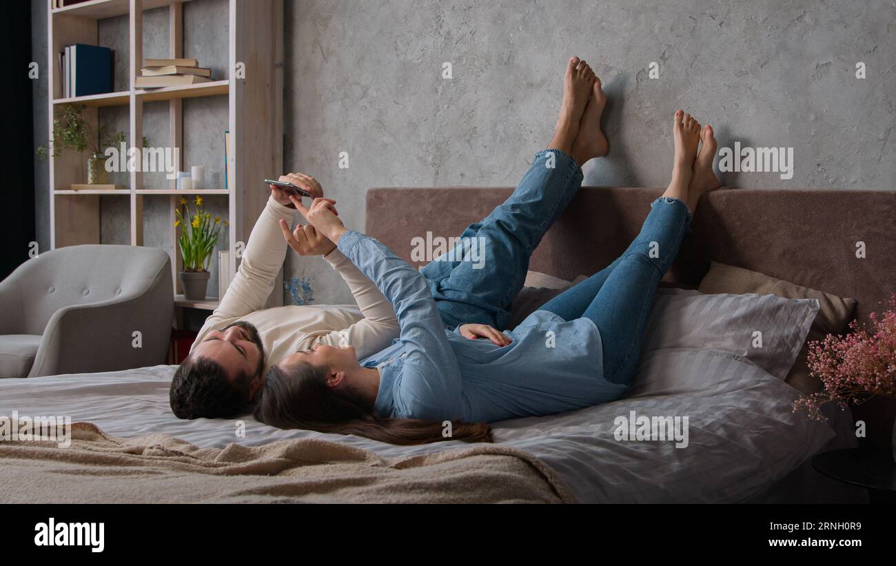 Carefree Caucasian couple in love lying down kick up feet on bed family ...
