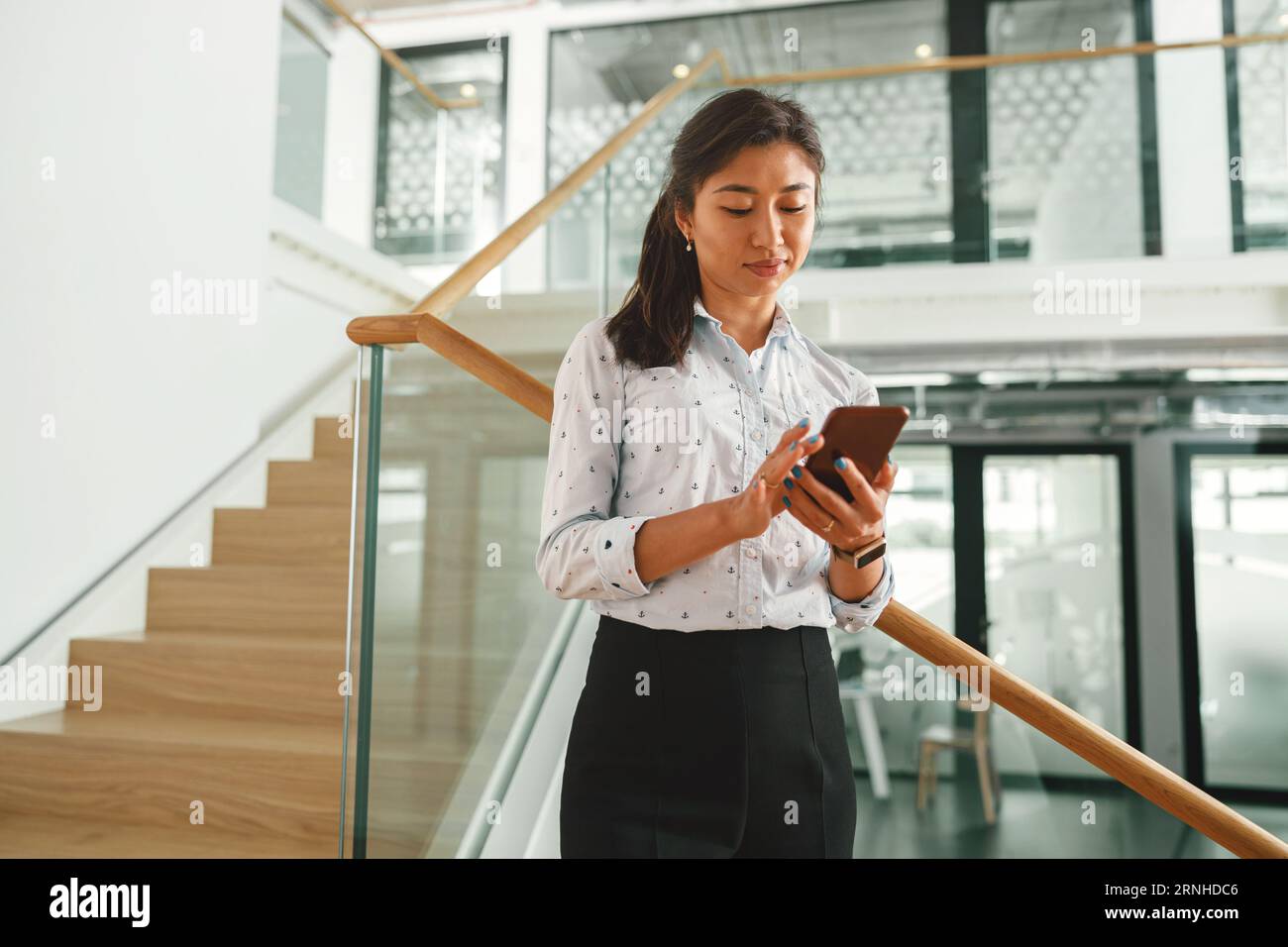 Stylish woman sales manager looking on smartphone standing on modern ...