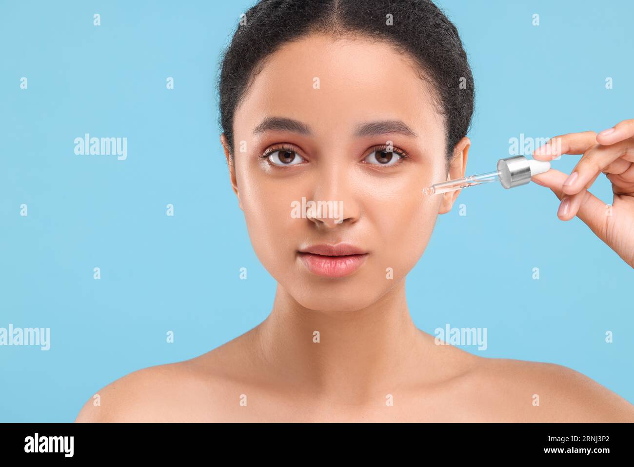 Beautiful woman applying serum onto her face on light blue background ...