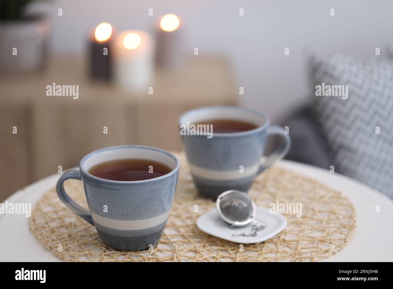 Cups of tea and snap infuser with dry leaves on white coffee table ...