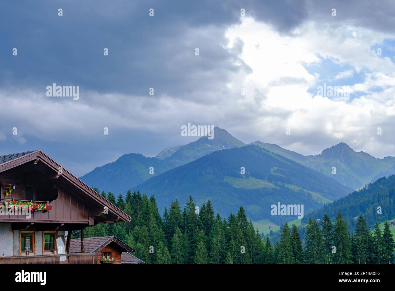 Traditional Austrian Wooden house with flowers on balcony, tall trees ...