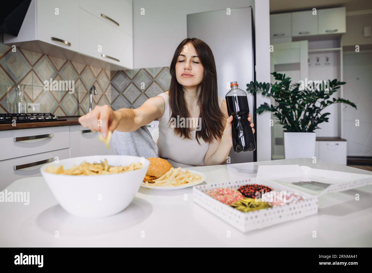 A woman eats junk food at home in the kitchen Stock Photo - Alamy
