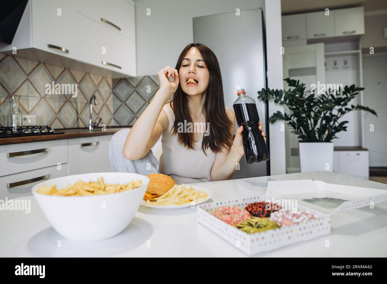 A woman eats junk food at home in the kitchen Stock Photo - Alamy