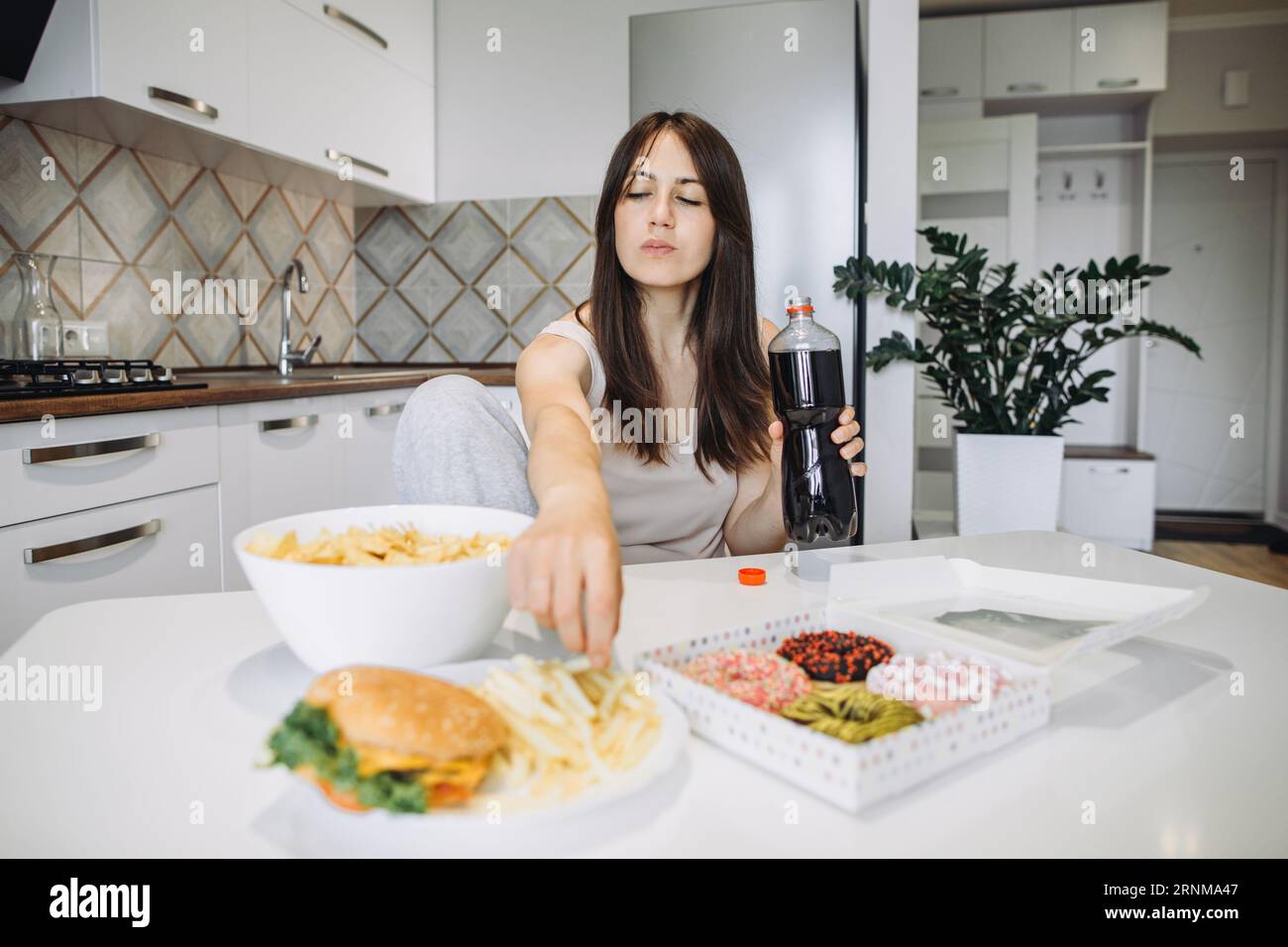 A woman eats junk food at home in the kitchen Stock Photo - Alamy