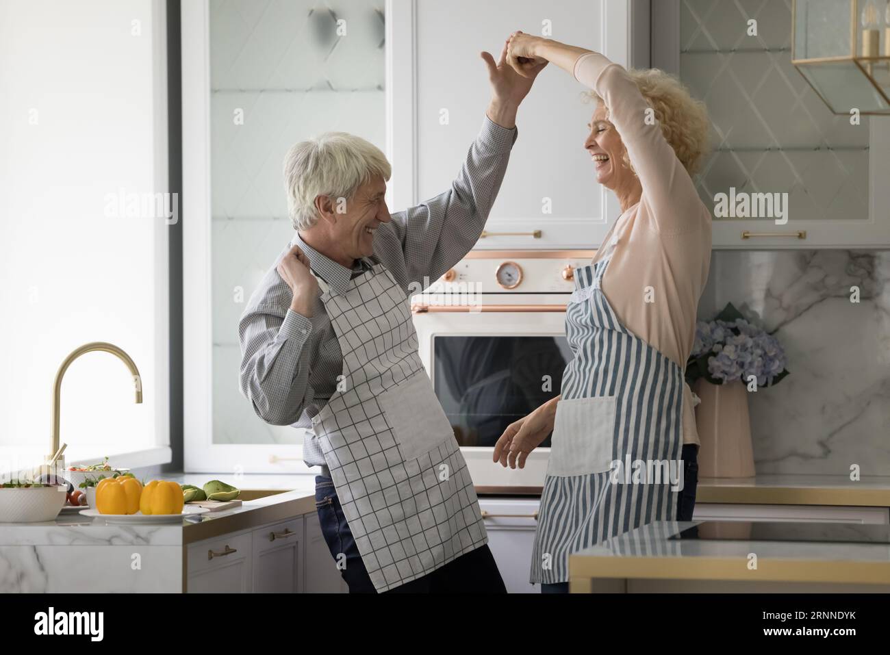 Happy cheerful active elder couple in aprons training social dance ...