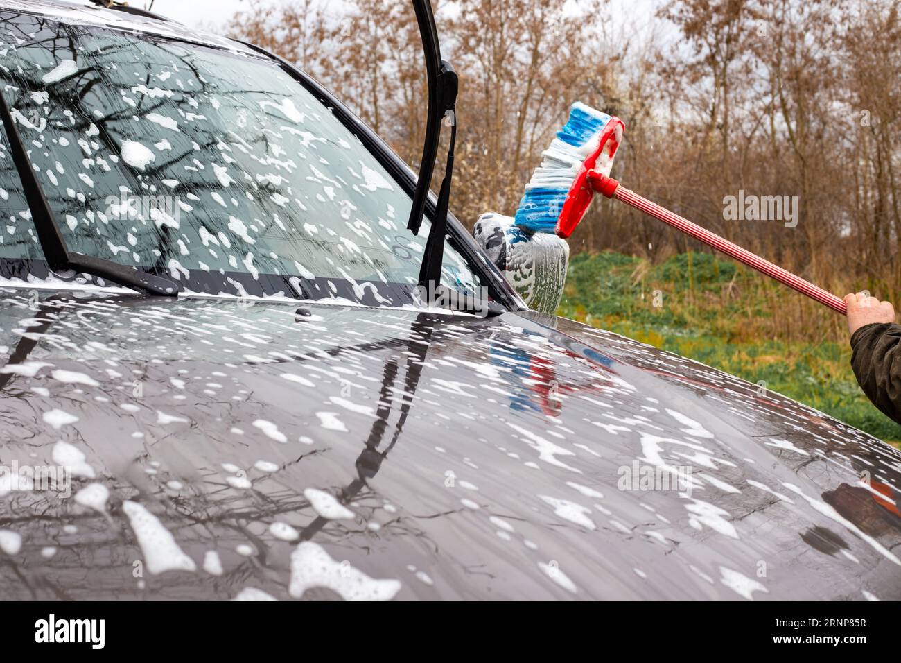 the hood and windshield of the car are wet with foam while washing with ...