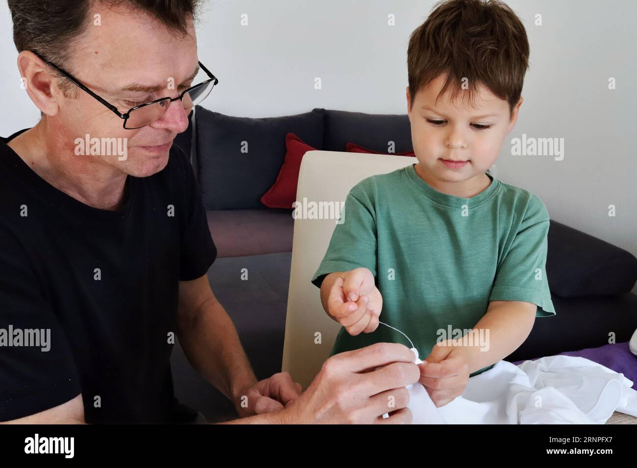 Father teaching his son how to sew on a button. Shot at home Stock ...