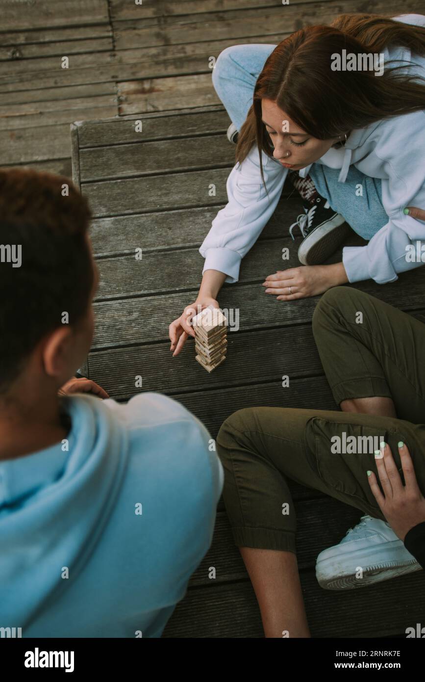 Three friends playing jenga on the wooden bench Stock Photo - Alamy