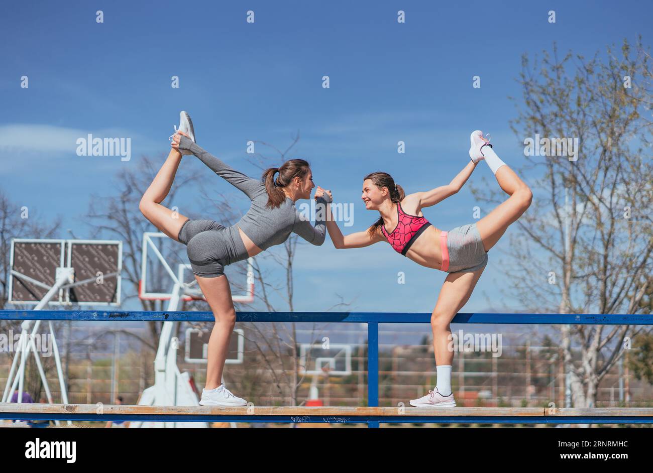 Flexible girls standing on bench on one leg faced to each other while ...