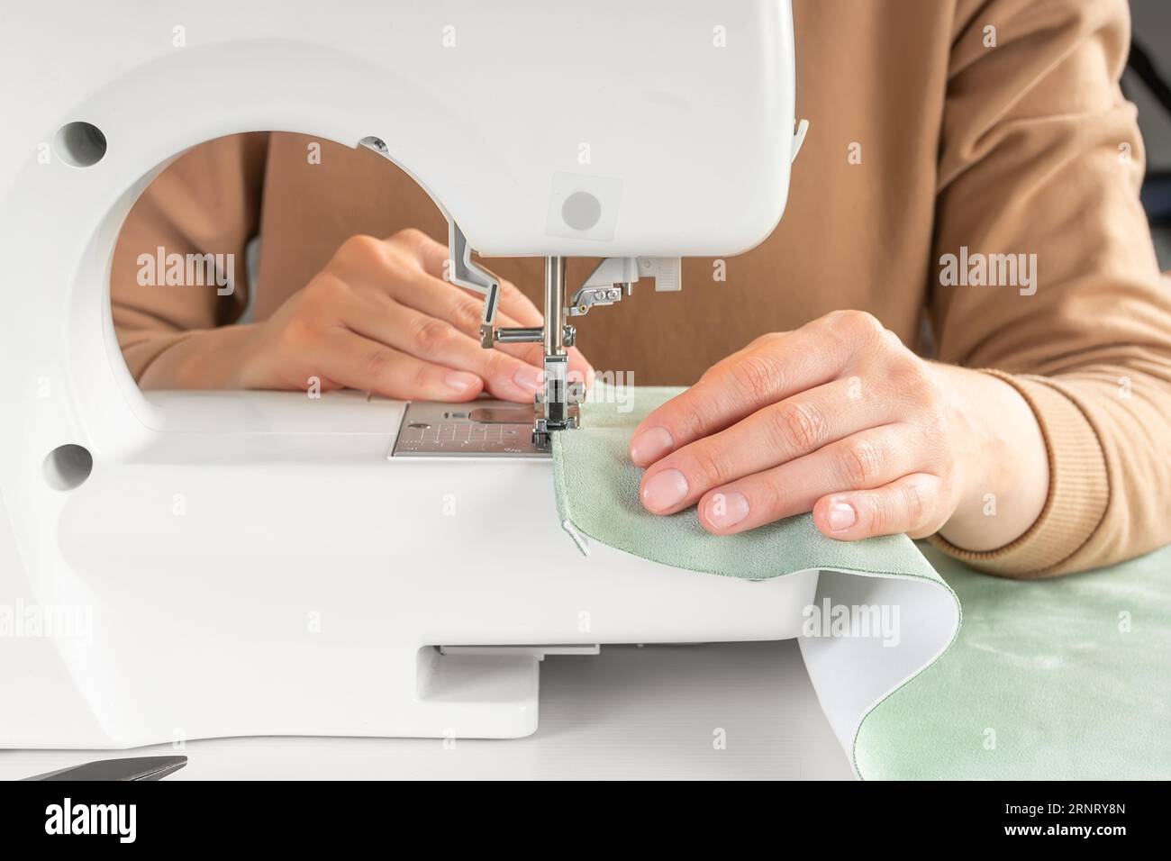 Tailor hands stitching green fabric on modern sewing machine at workplace in atelier. Women's ...
