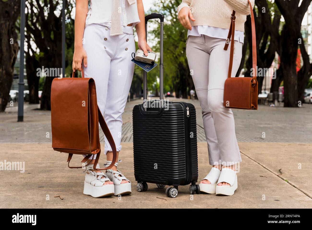 Low section two young women standing with black suitcase their leather ...