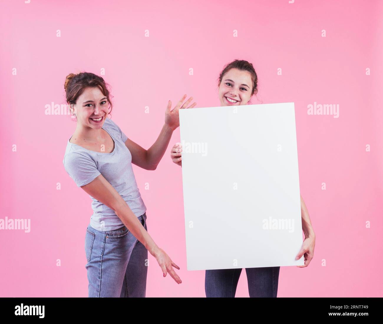 Woman presenting blank placard hold by her friend against pink ...