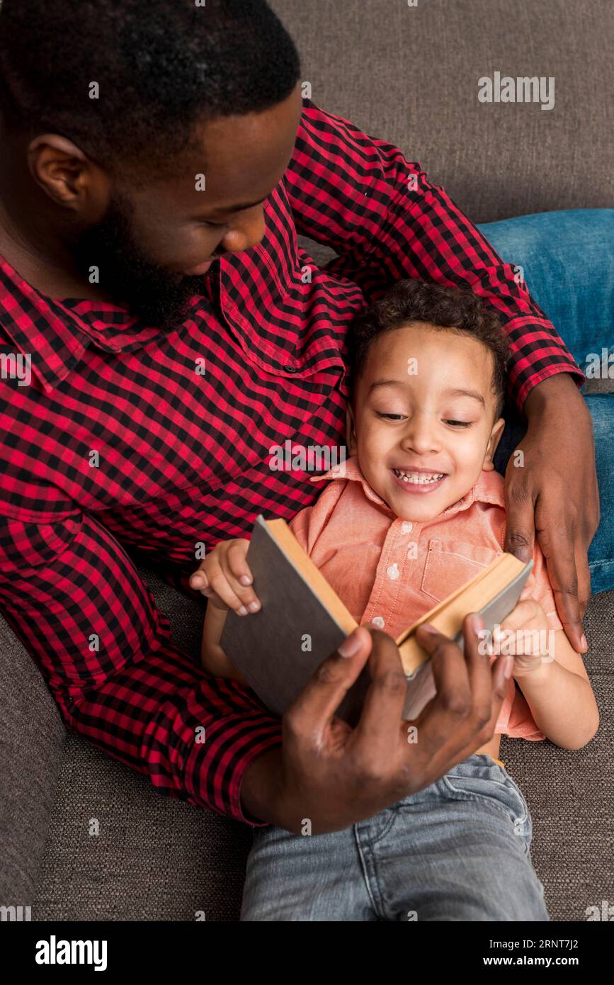 Black father cute son reading book couch Stock Photo - Alamy