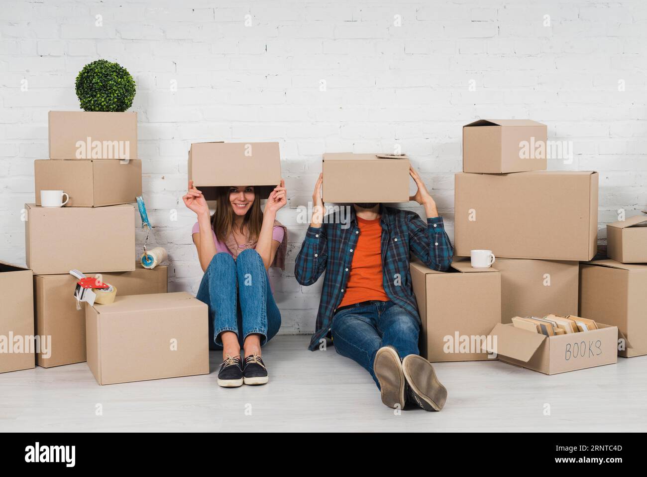 Young couple hiding their face sitting cardboard boxes their new house ...