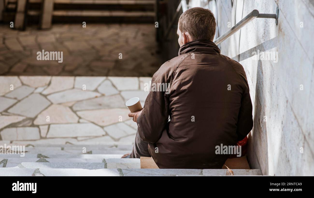 Back view homeless man with cup stairs Stock Photo - Alamy