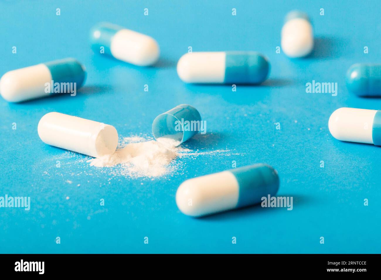 Broken white antibiotic capsule blue background Stock Photo - Alamy