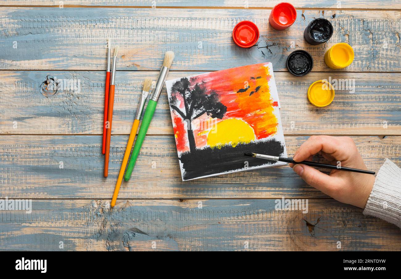 Elevated view human hand painting sunset seen with paint brush wooden ...