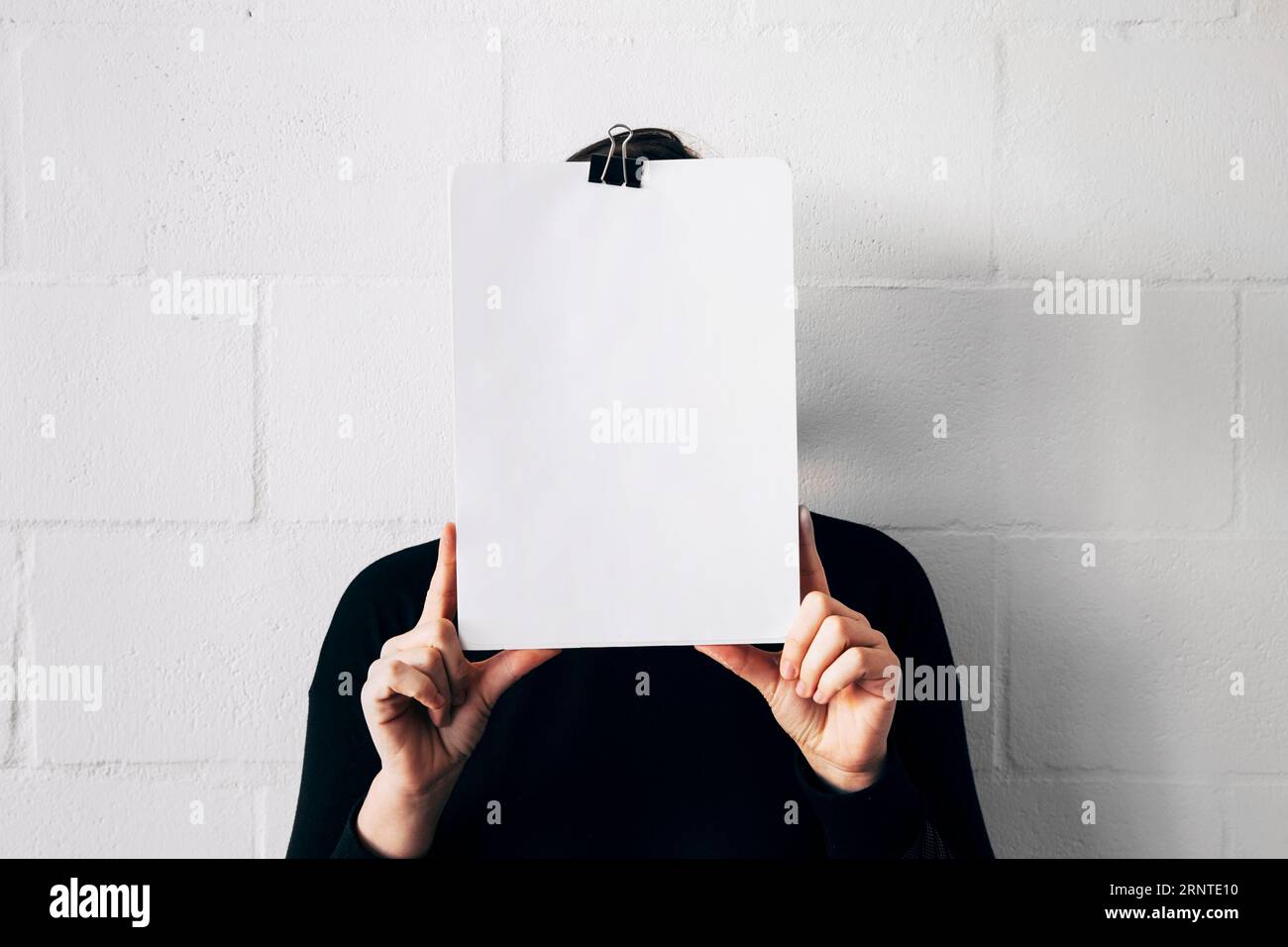 Female holding white paper front her face against white wall Stock ...