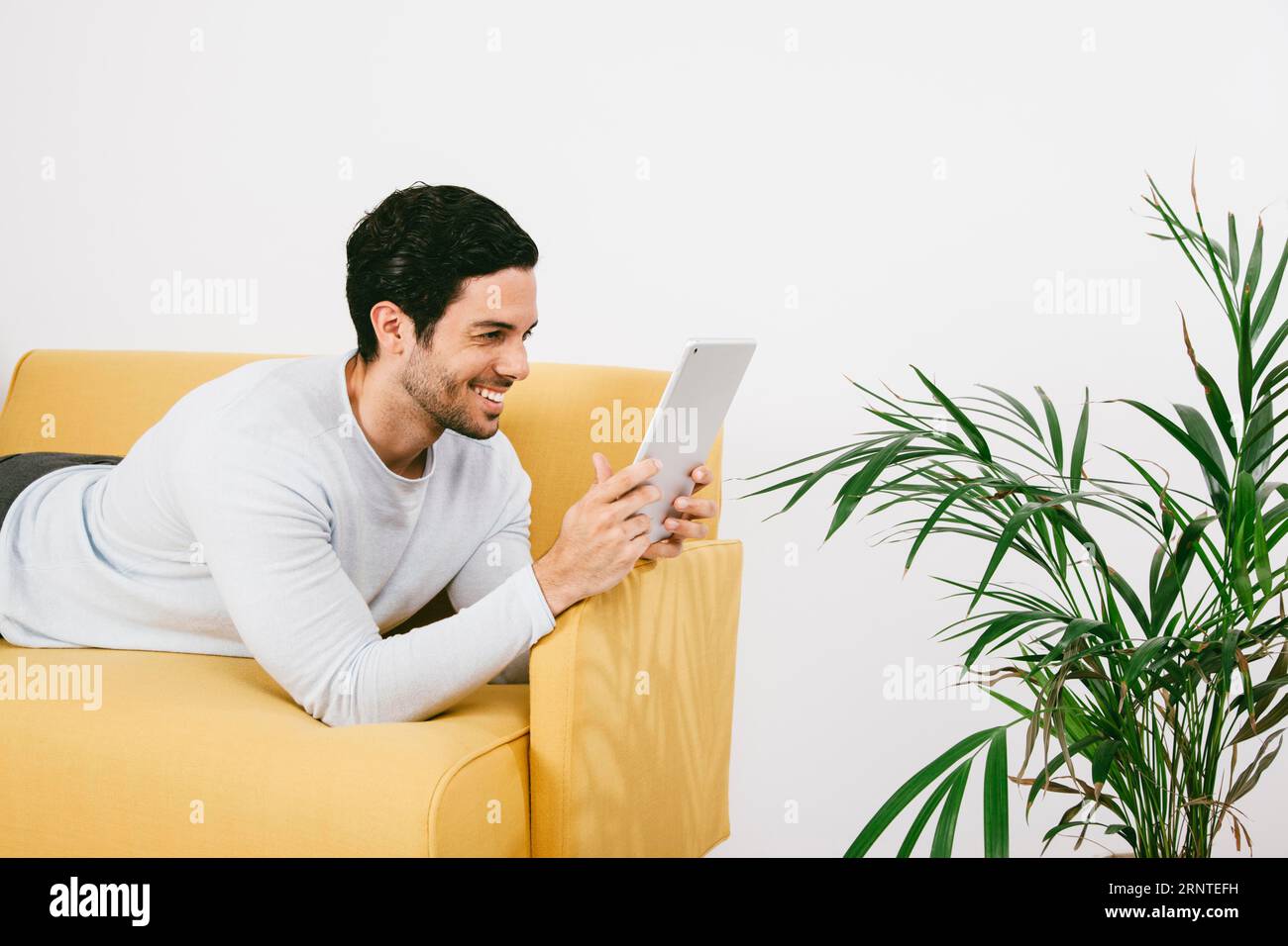Happy young man laying sofa with tablet Stock Photo - Alamy