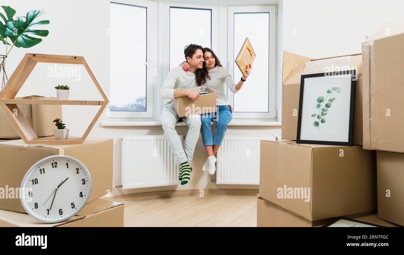 Portrait loving young couple sitting window sill new apartment looking ...