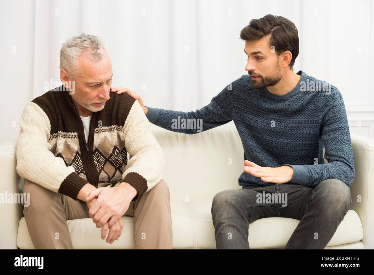 Young guy with hand shoulder aged sad man sofa Stock Photo - Alamy
