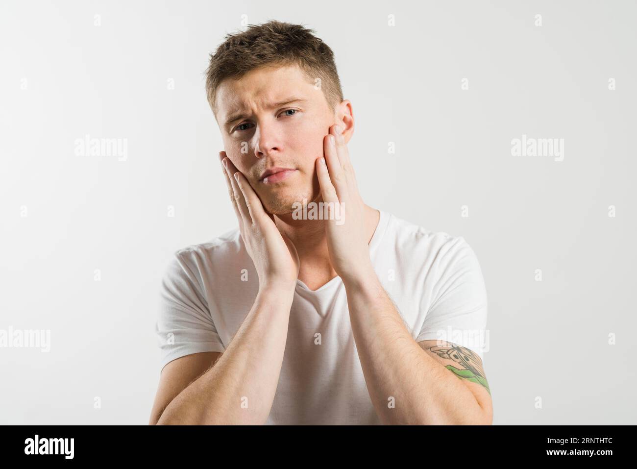 Young man touching his cheeks with two hands against white background ...