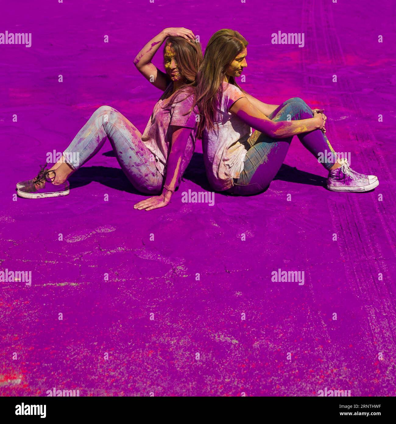 Young women sitting back back purple holi color Stock Photo - Alamy