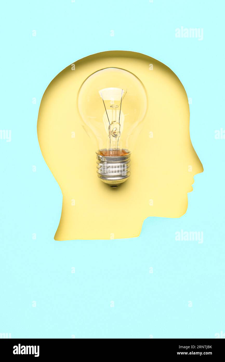 Light bulb visible through cut blue paper in shape of human head on ...