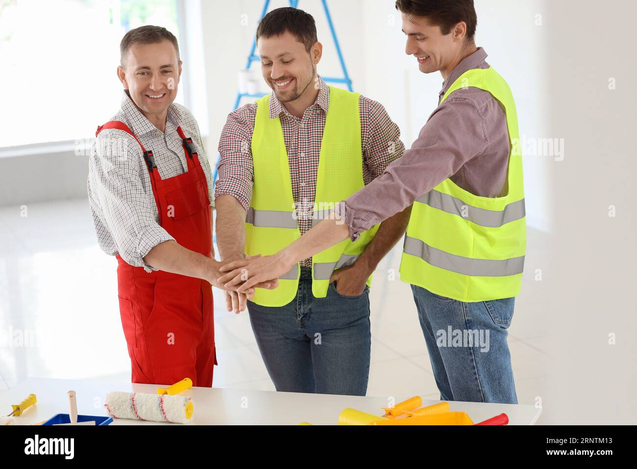 Team of male builders putting hands together in room Stock Photo - Alamy