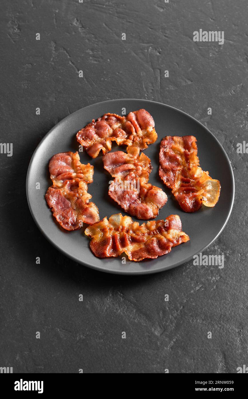 Roasted bacon on plate over black stone background. Close up view Stock ...