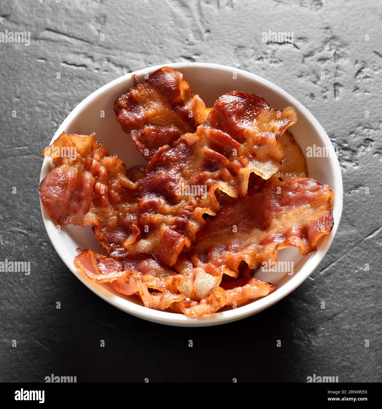 Roasted bacon in bowl over black stone background. Close up view Stock ...