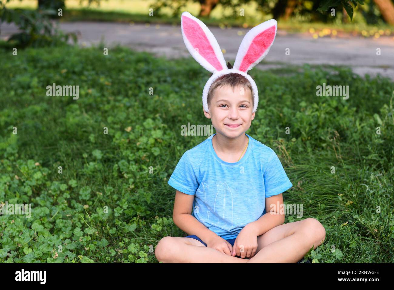 funny boy smiles sitting on the grass. he put on the ears of a hare ...