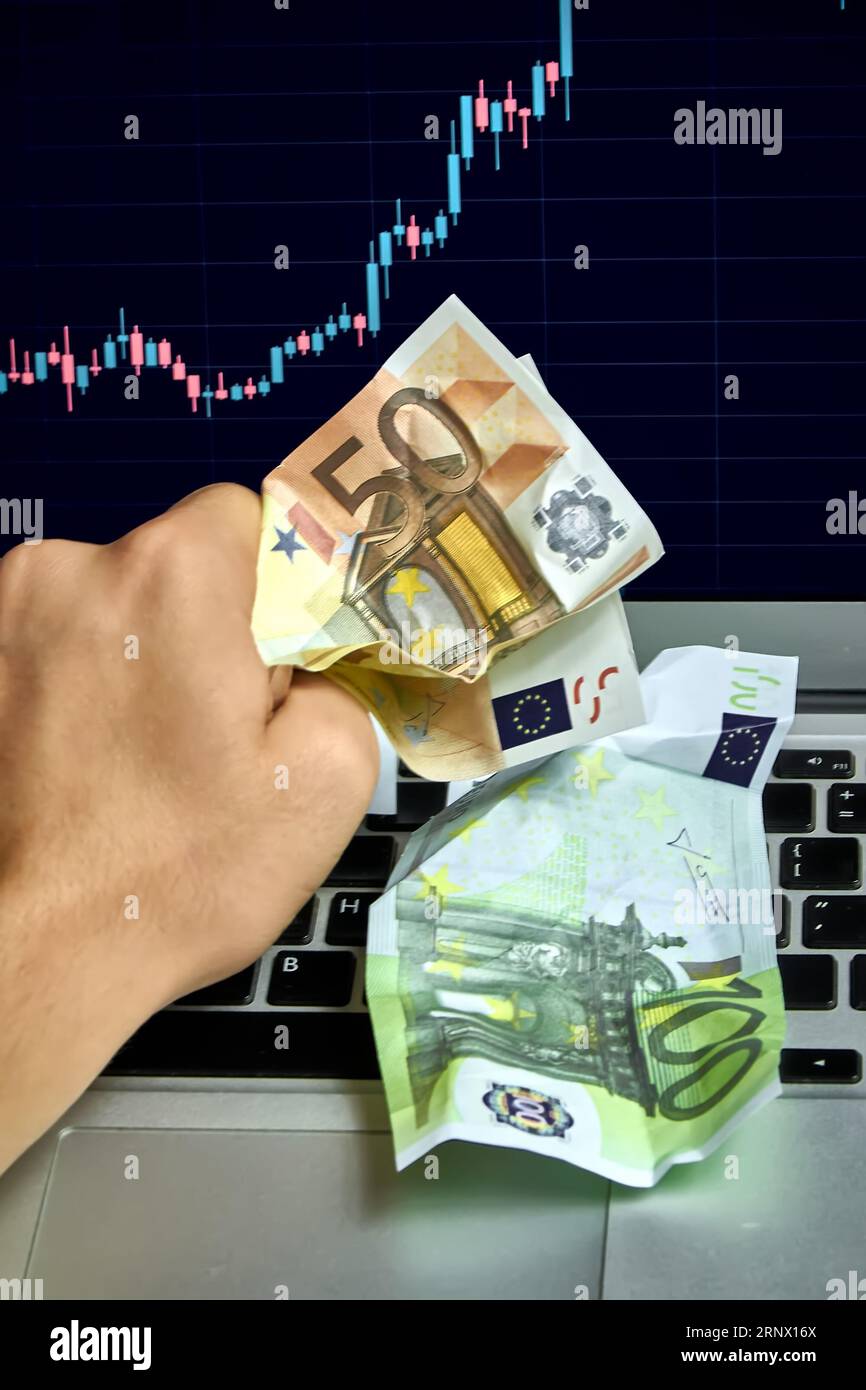 A hand clutching paper bills in the background of a stock market chart ...